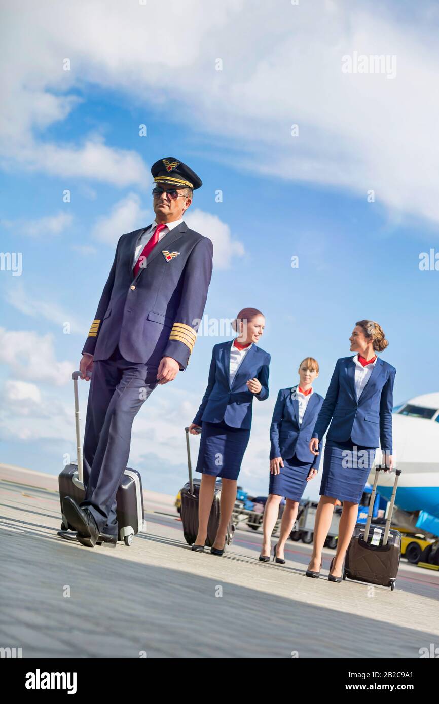 Portrait of mature pilot walking with three young beautiful flight ...