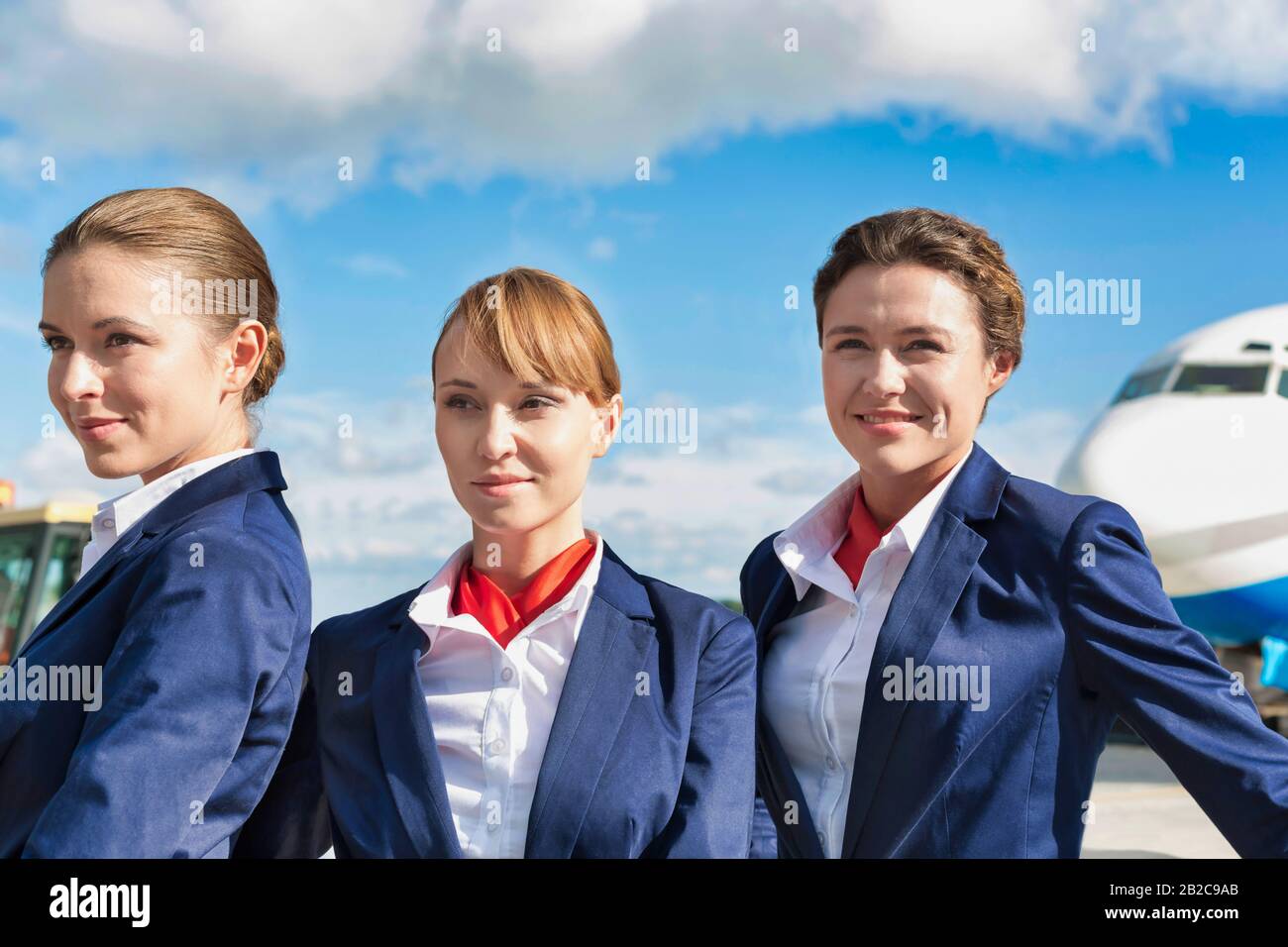 Portrait of three young attractive flight attendants standing against ...