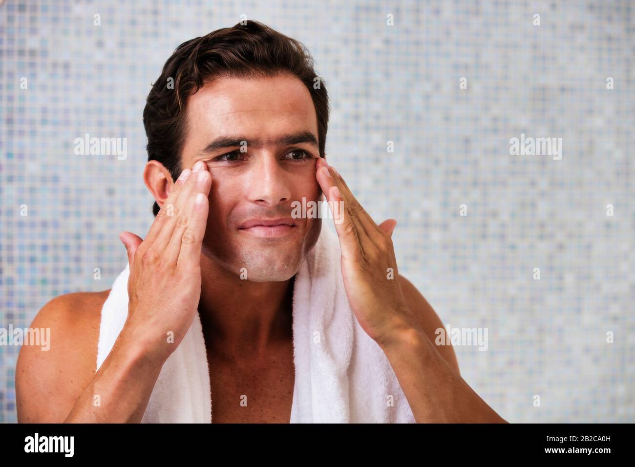 Portrait of attractive man cleansing his face with facial foam in the ...