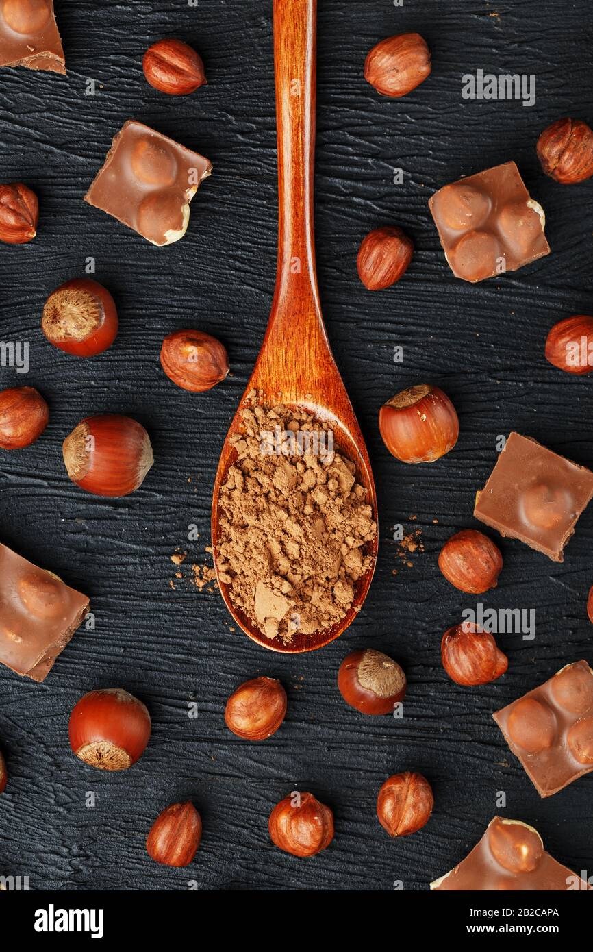 Chocolate with hazelnuts and a wooden spoon with cocoa on a dark ...