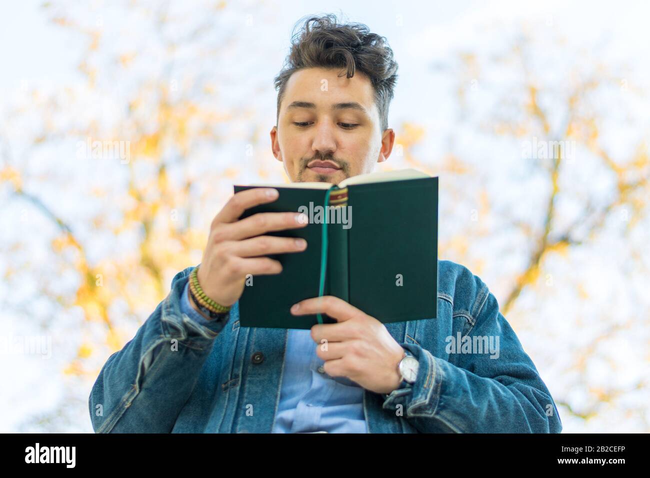 Handsome young man reading a book in a park. Portrait of a young man ...