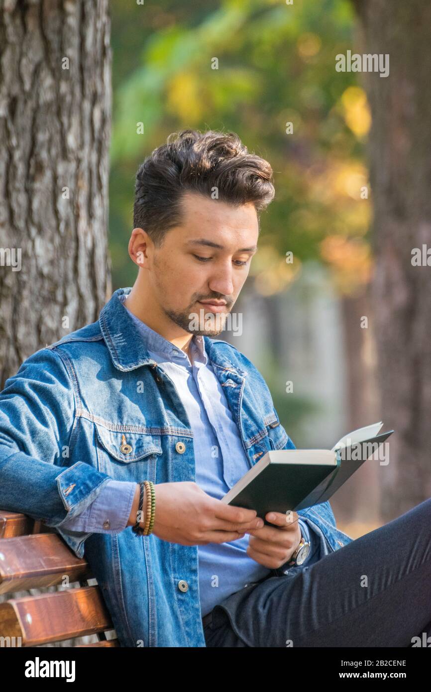Handsome young man reading a book in a park. Portrait of a young man ...