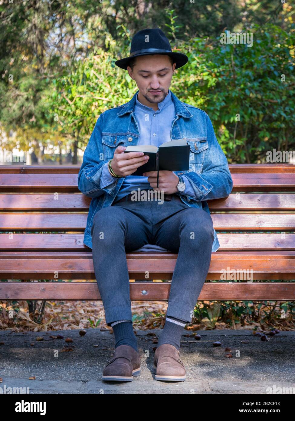 Handsome young man reading a book in a park. Portrait of a young man ...