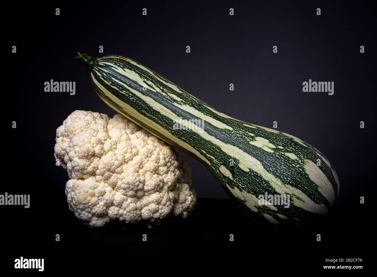 Courgette vegetable resting on cauliflower in studio setting with dark ...