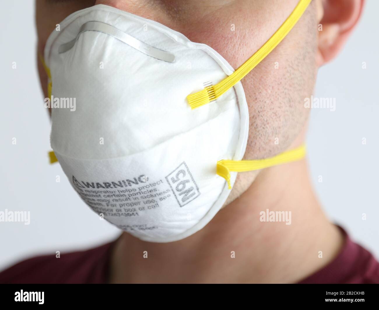 A man is shown wearing a protective N95 white dusk mask up close, set ...