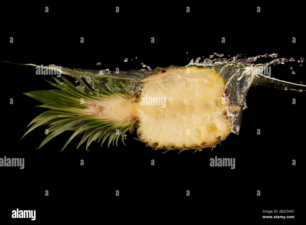 Half of juicy pineapple falling into transparent water on black ...