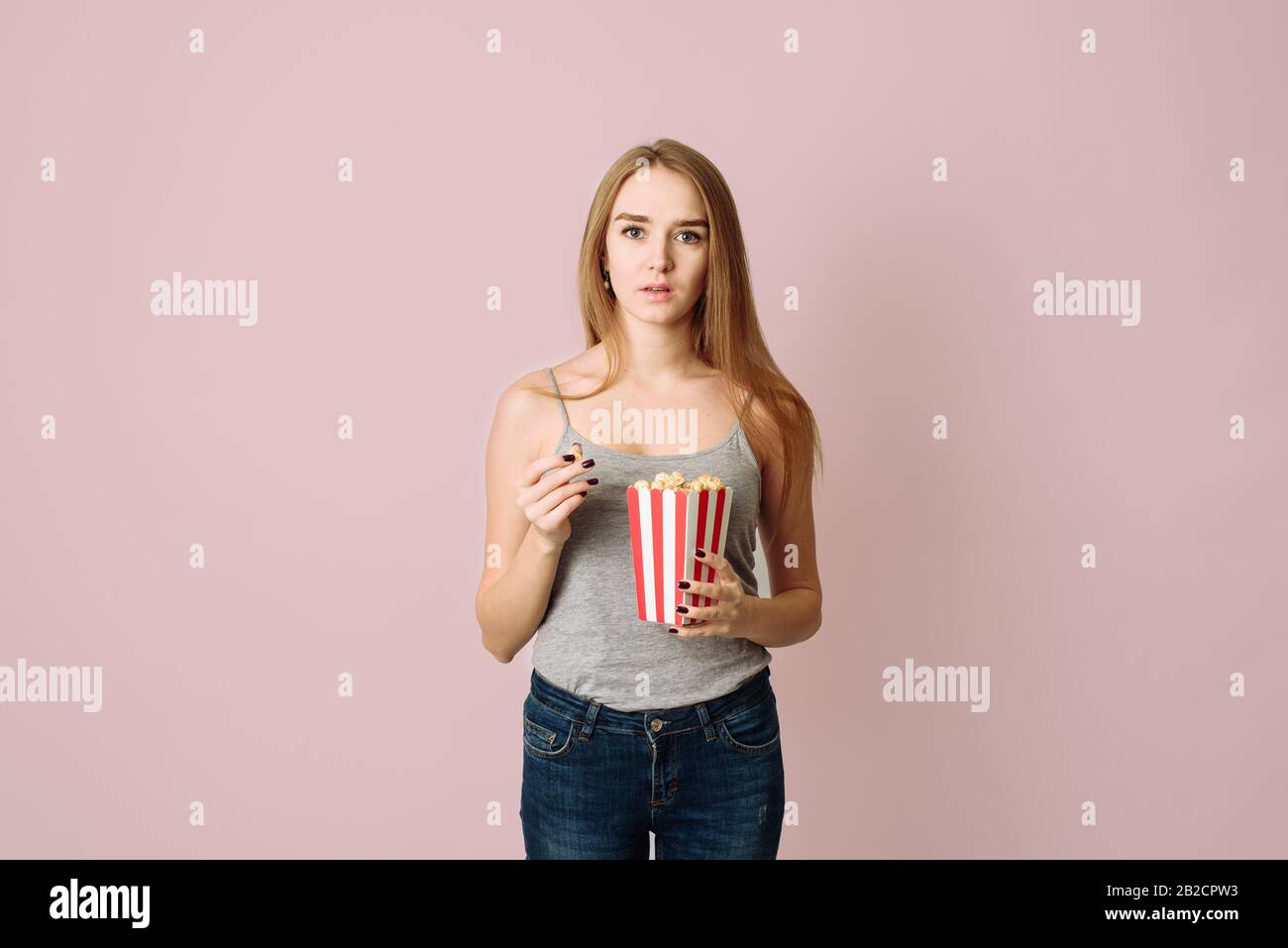 Surprising woman eating popcorn. Girl holding big striped box with ...