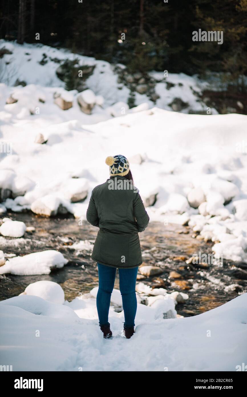 Back of a girl standing near winter river. Back view of a girl with hat ...