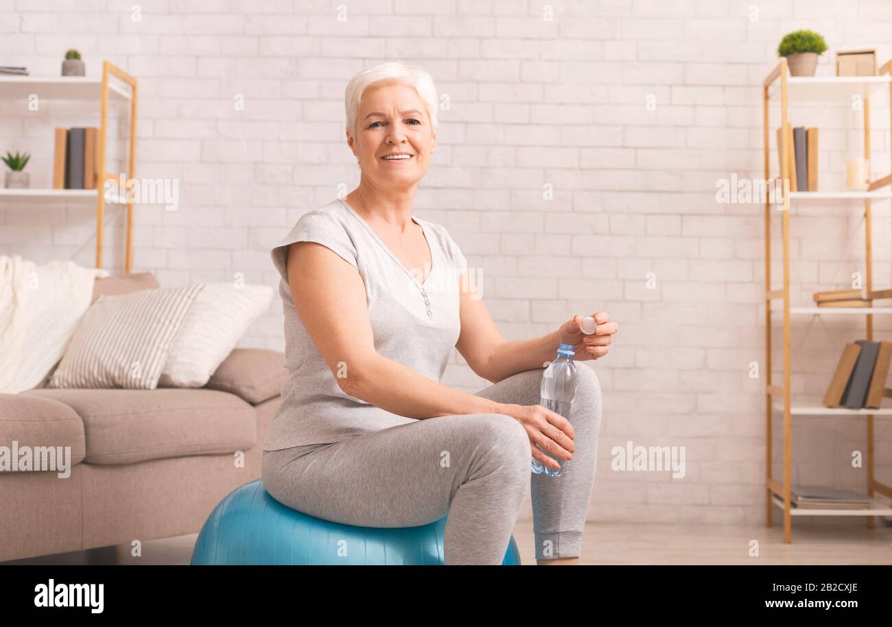 Cheerful senior woman drinking water on fitball, free space Stock Photo ...
