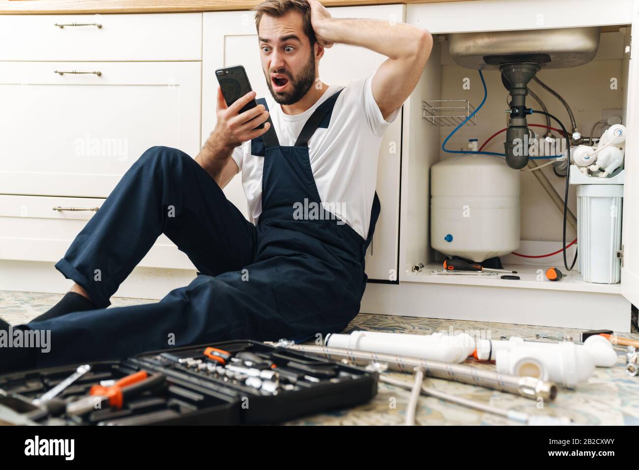Image of young shocked emotional man plumber work in uniform indoors ...