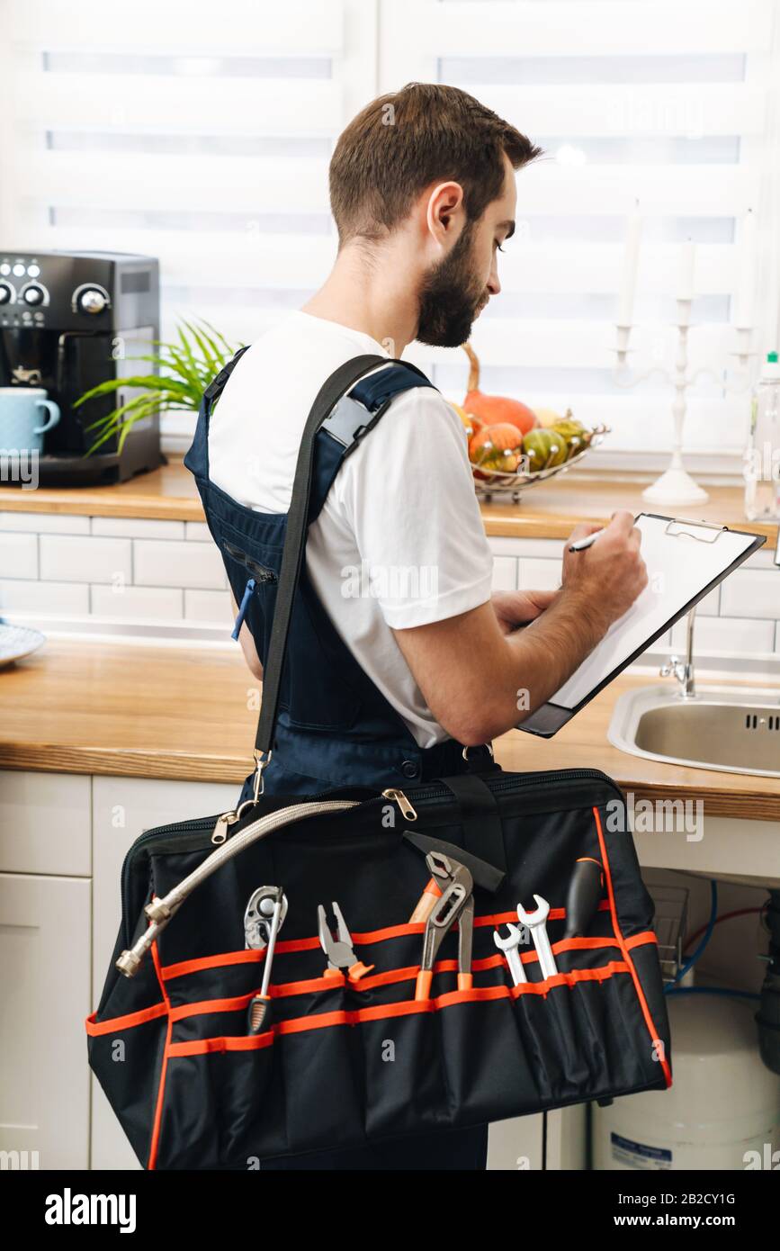 Image of young man plumber work in uniform indoors holding bag with ...