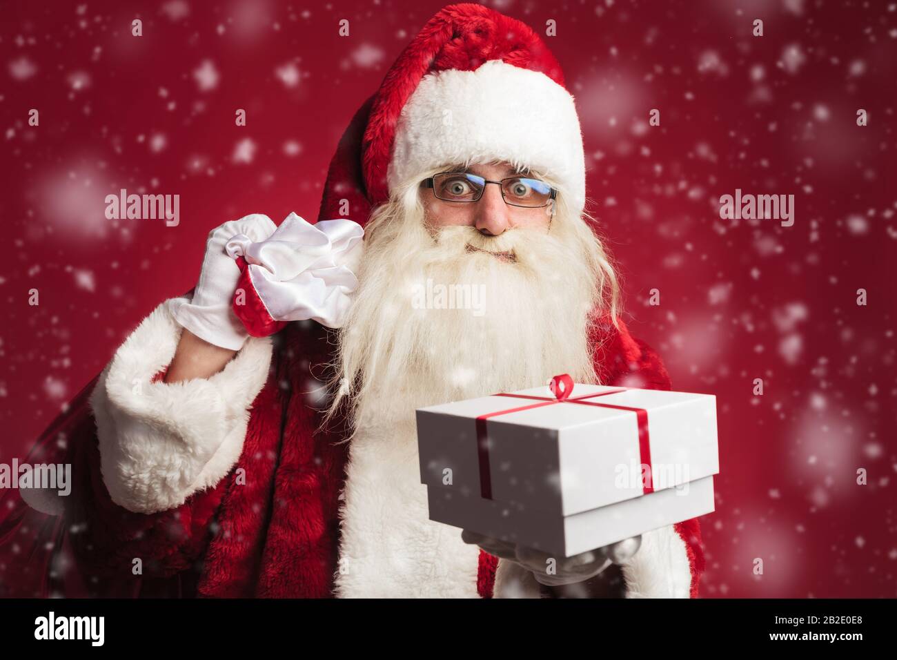 santa claus holding bag on shoulder and offering a gift box on red ...