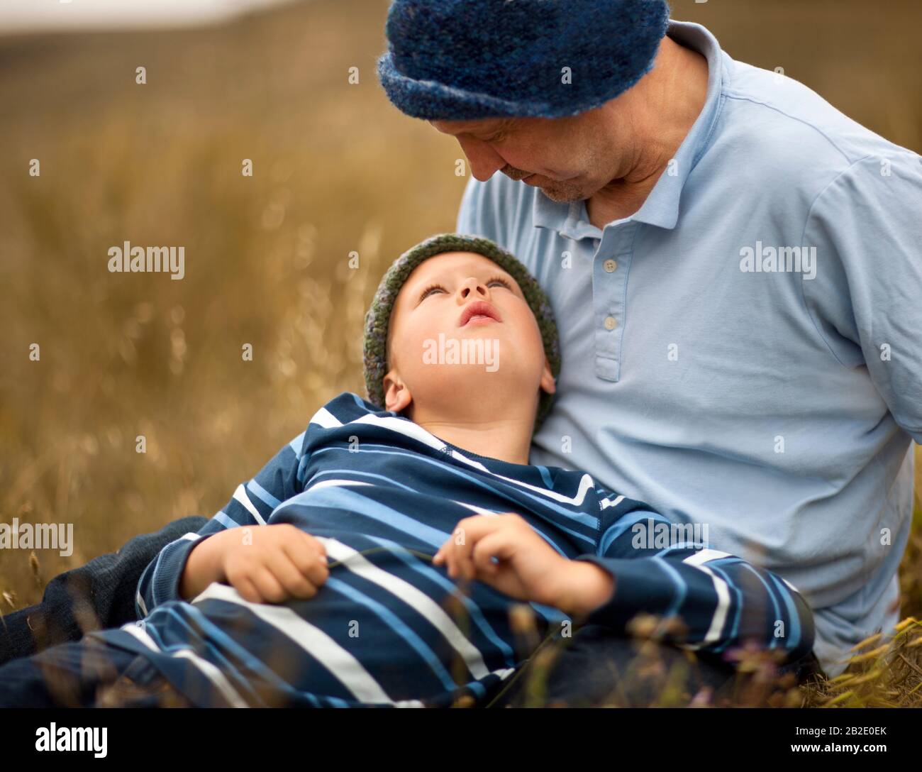 Young boy lying in his father's lap in a field Stock Photo - Alamy