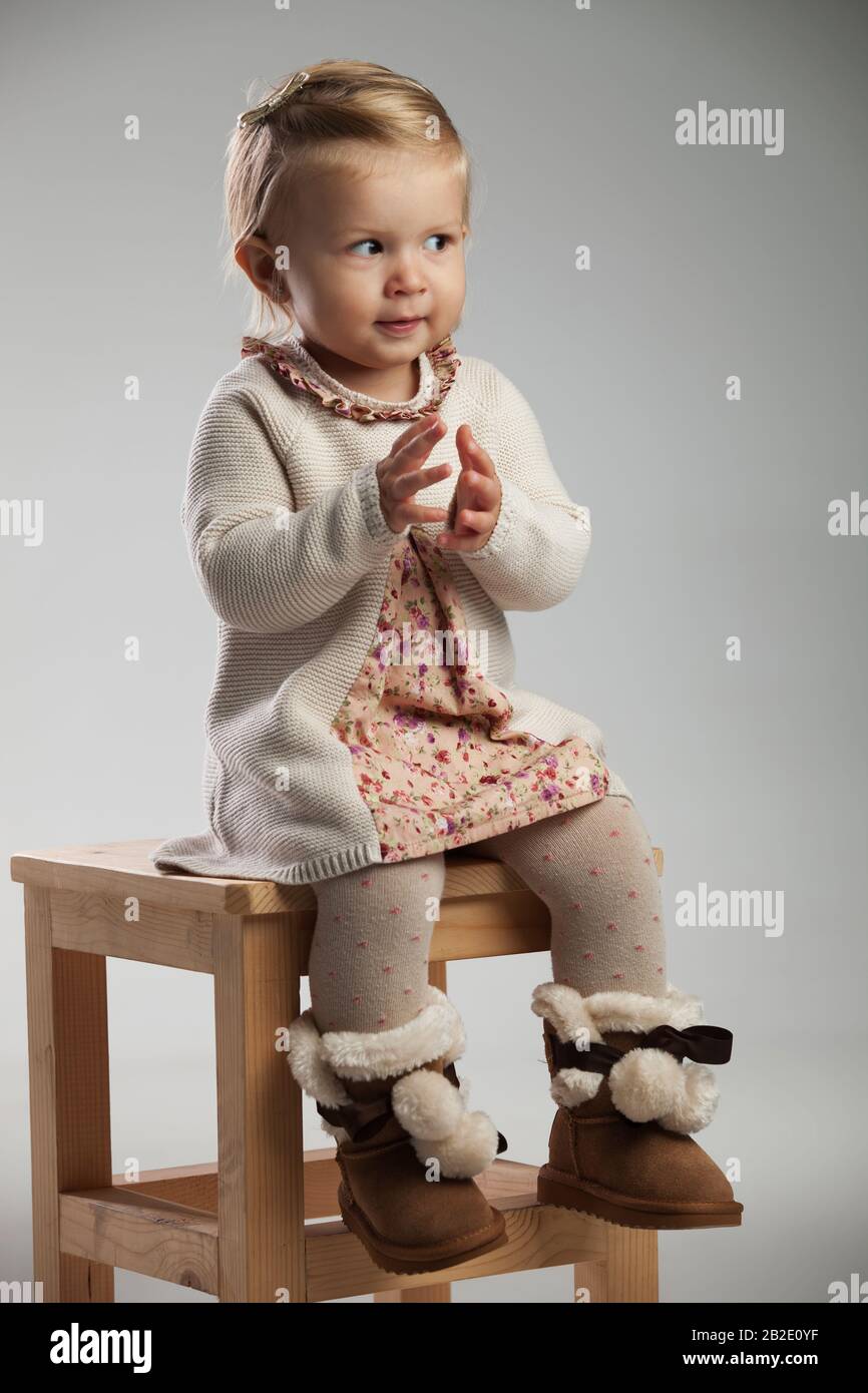 little seated girl is expecting to clap her hands while seated on grey ...