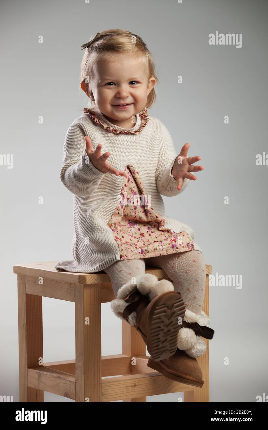 eager little girl is sitting on a chair on grey background Stock Photo ...