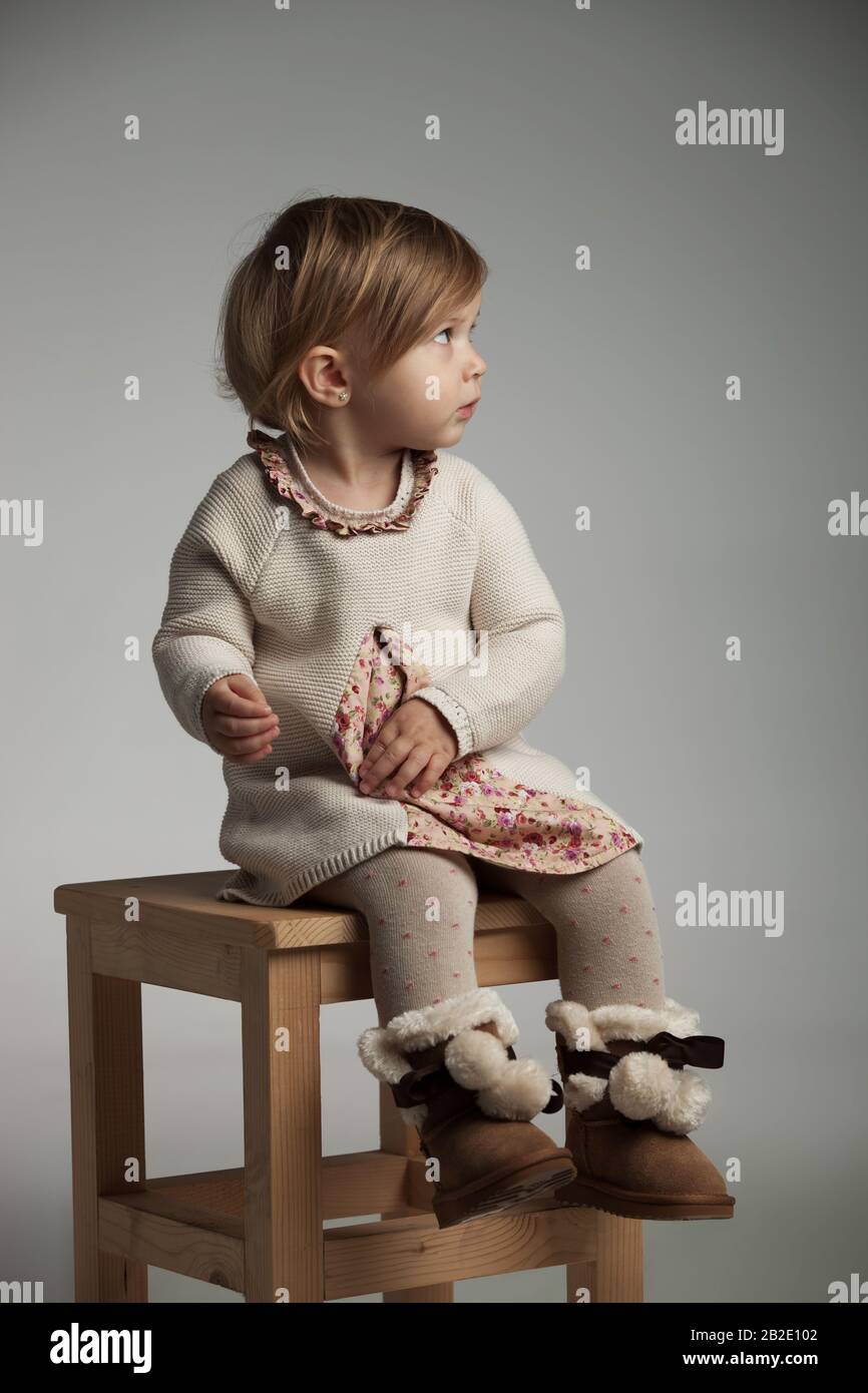 side view of a cute little girl sitting on a chair on grey background ...