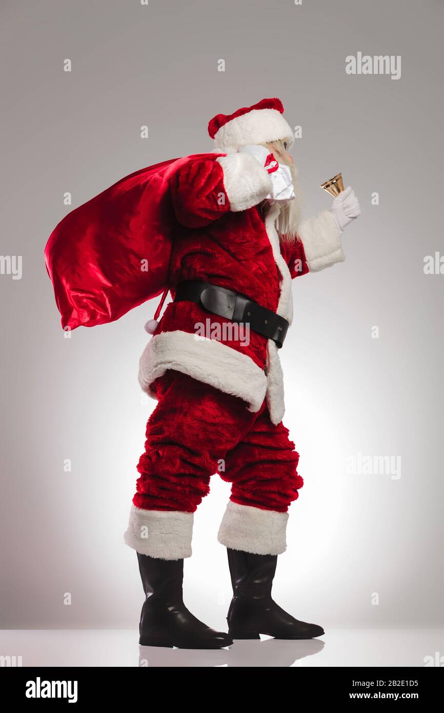 side view of santa claus ringing bell with bag on shoulder on grey ...