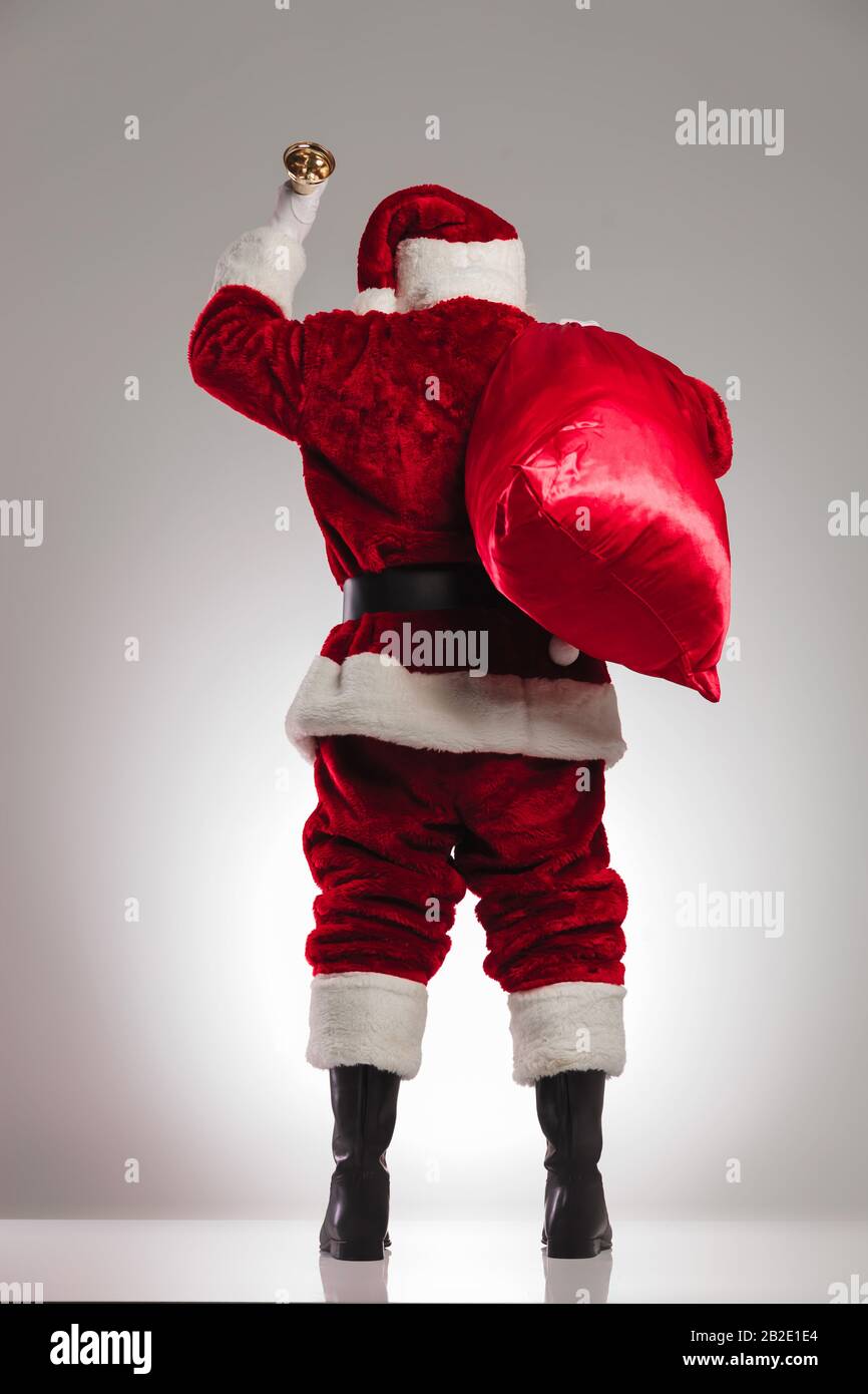 back view of santa claus ringing bell with bag on shoulder on grey ...