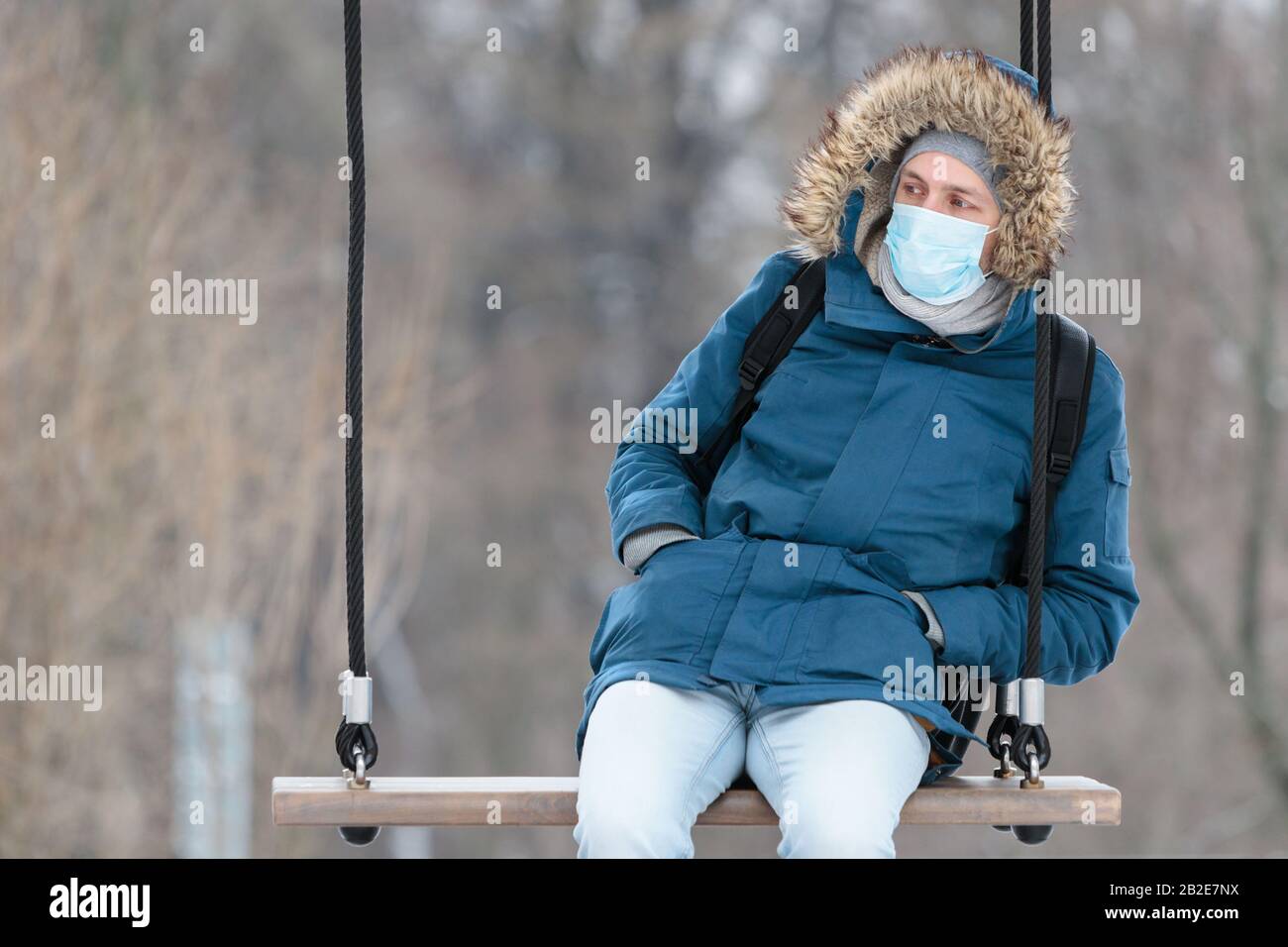Sick man with a hood sitting alone on a swing, wearing protective ...