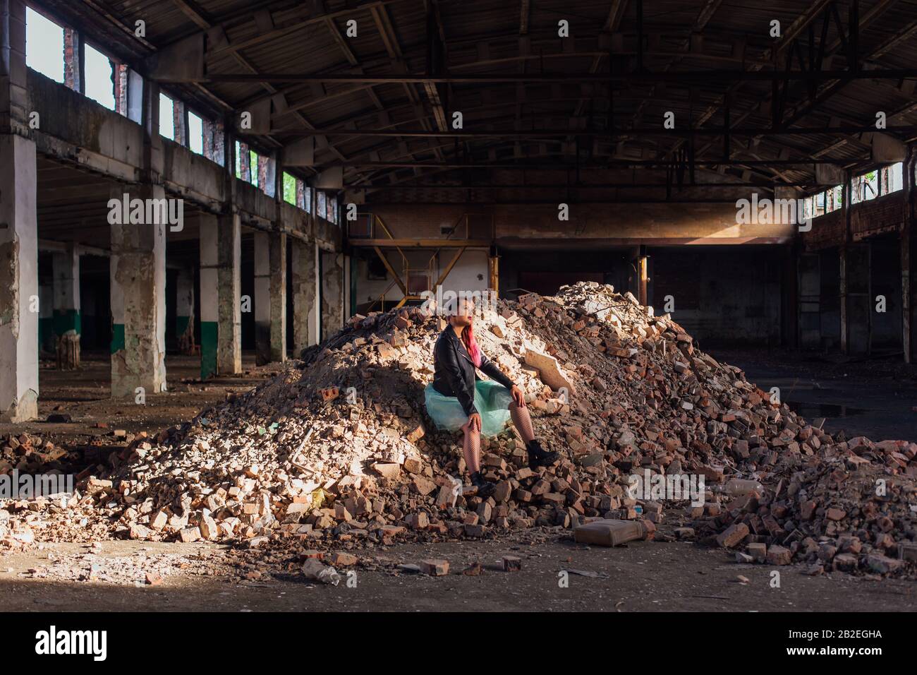 Young girl with pink hair sitting on bricks in a collapsed building ...
