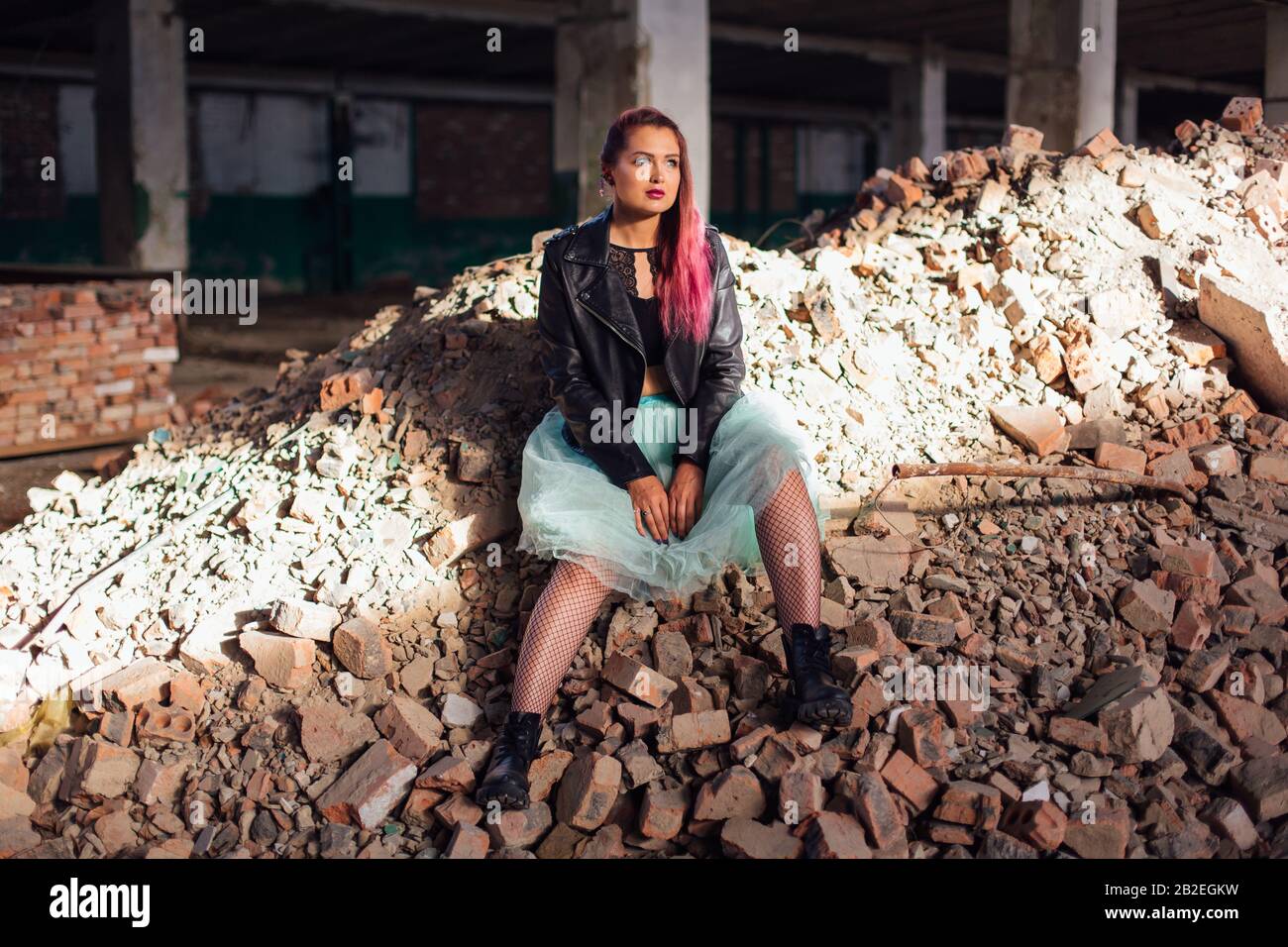 Young girl with pink hair sitting on bricks in a collapsed building ...