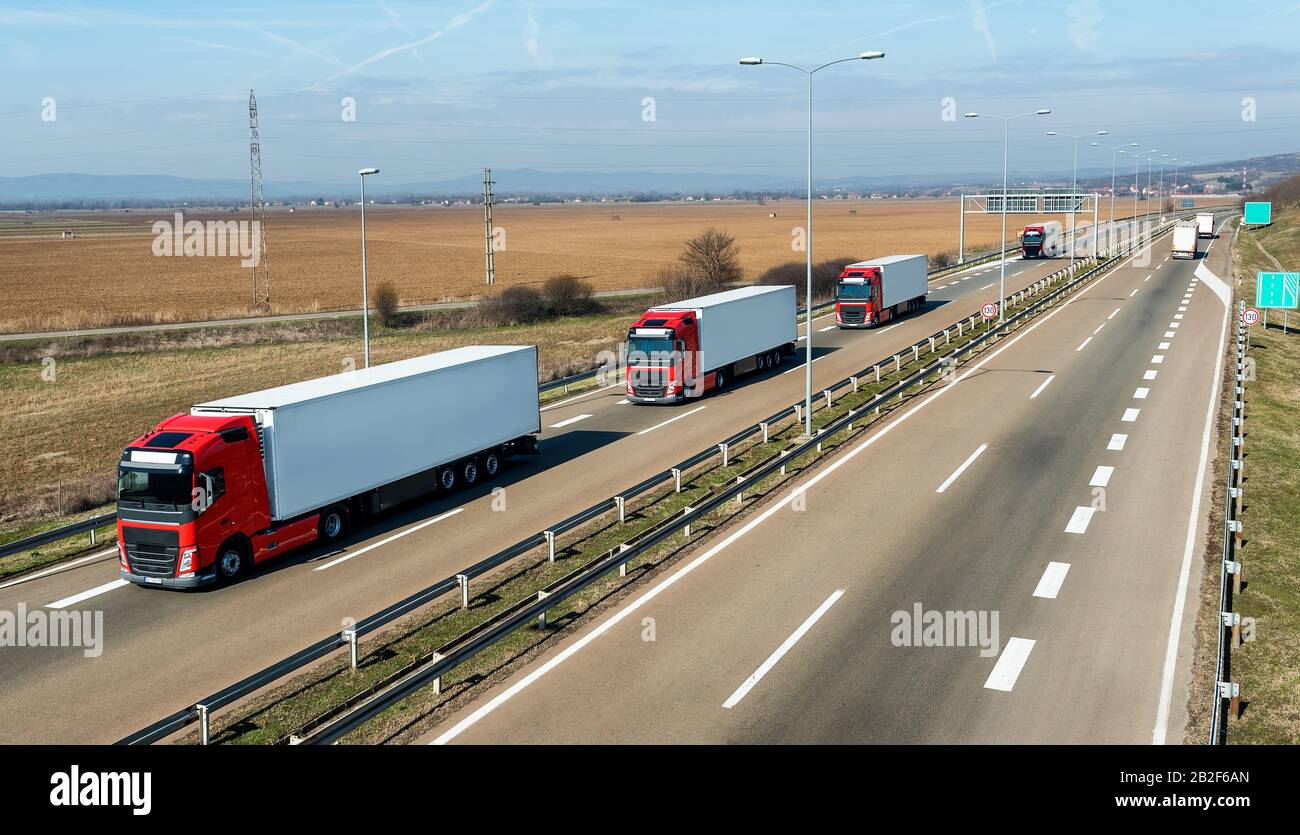 Convoy of transportation trucks passing on a highway on a bright blue ...