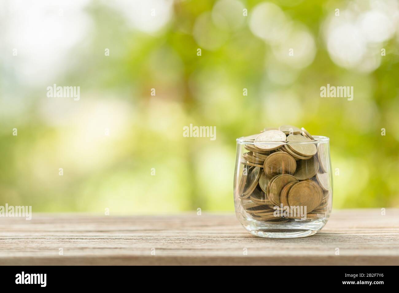 Close up coins in clear money jar on wooden table with green blur light ...