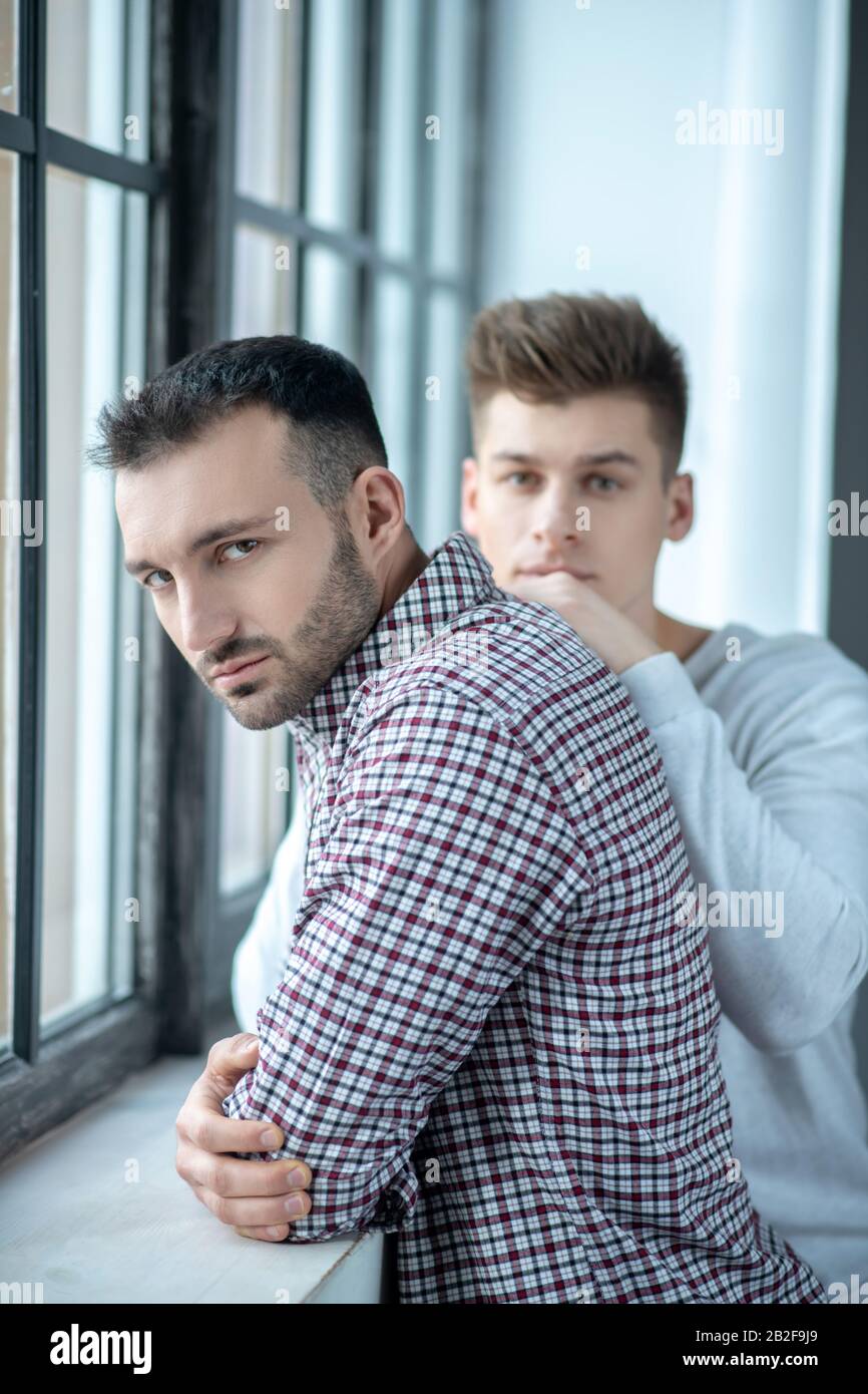 Two young men standing near the window feeling sad Stock Photo - Alamy