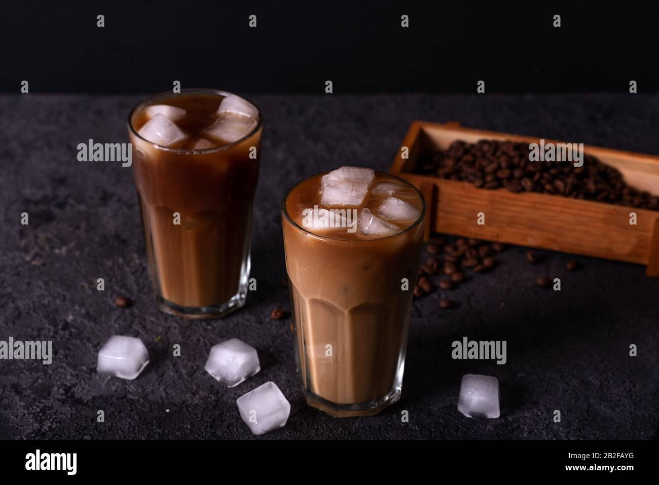 Iced coffee in a tall glass with cream poured over. Wood background ...