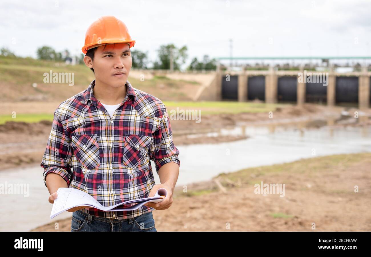 Asian young engineer working on site at the dam and control while ...
