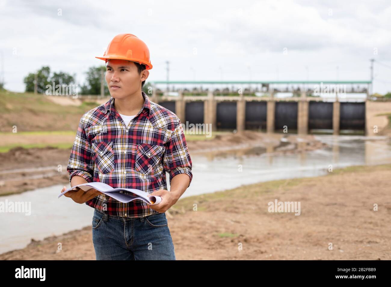 Asian young engineer working on site at the dam and control while ...