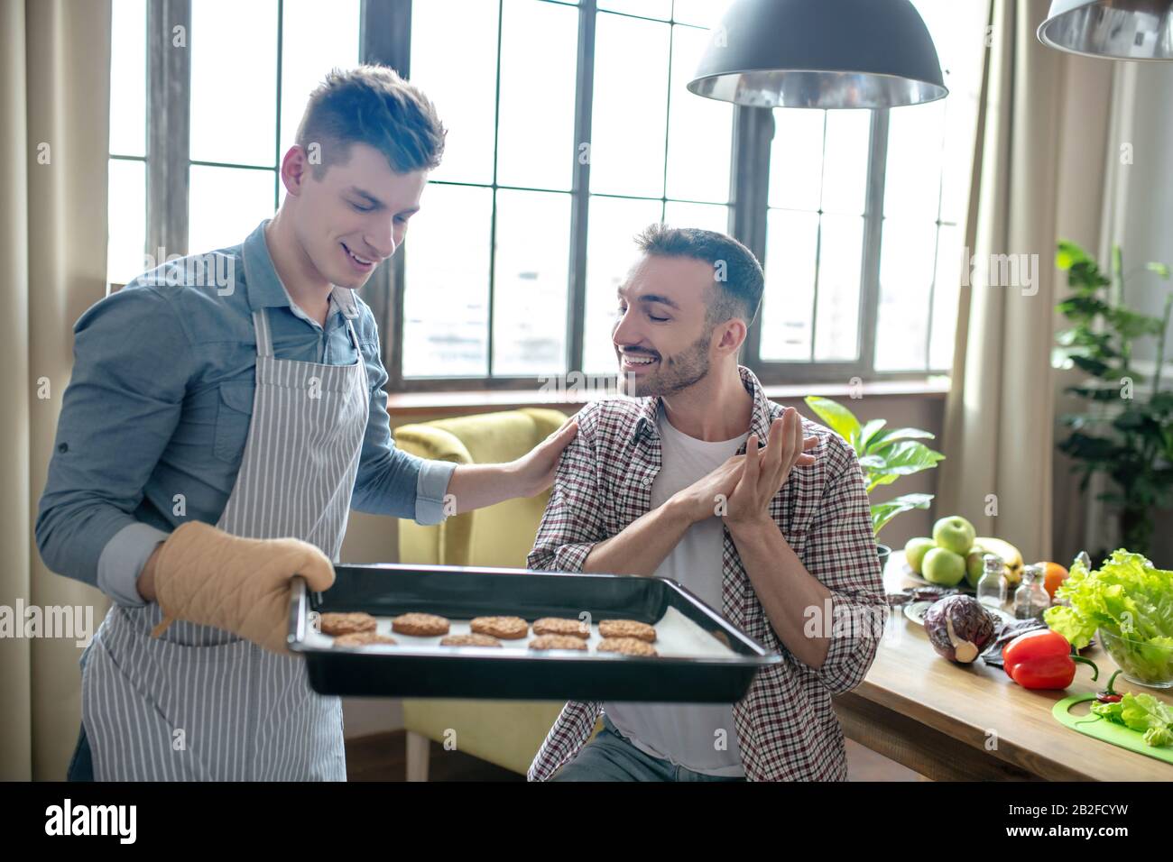 Man with a baking sheet showing pastries to a seated person Stock Photo ...
