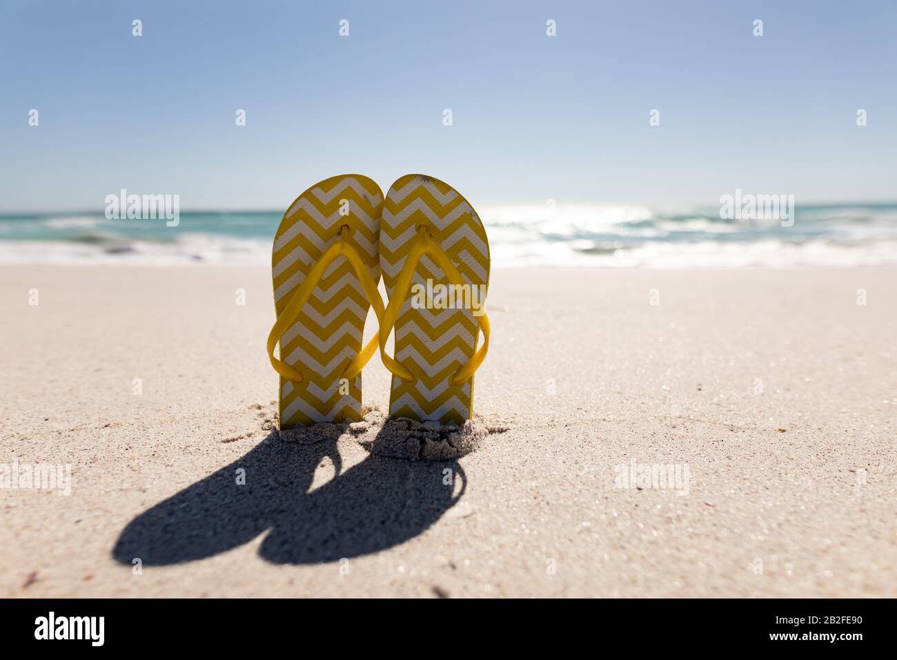 Pair of yellow and white zig zag patterned flip flops stuck in sand on ...