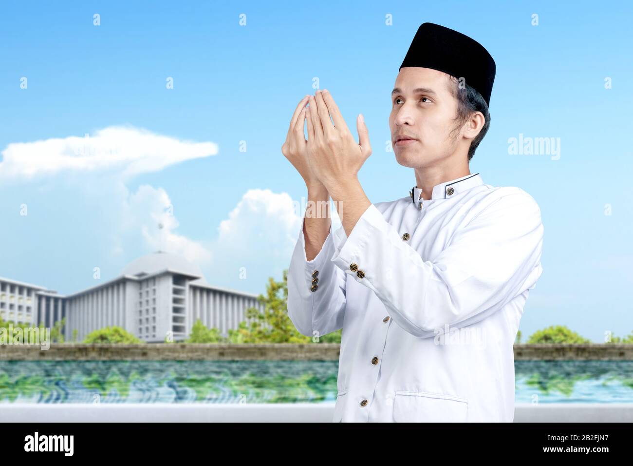 Asian Muslim man standing while raised hands and praying with mosque ...