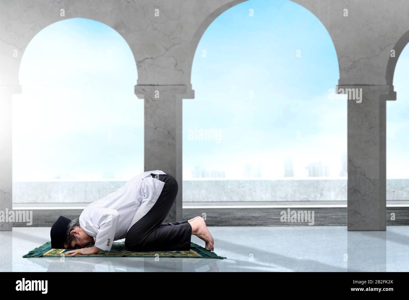 Asian Muslim man with a prayer rug in a praying position (salat) inside ...