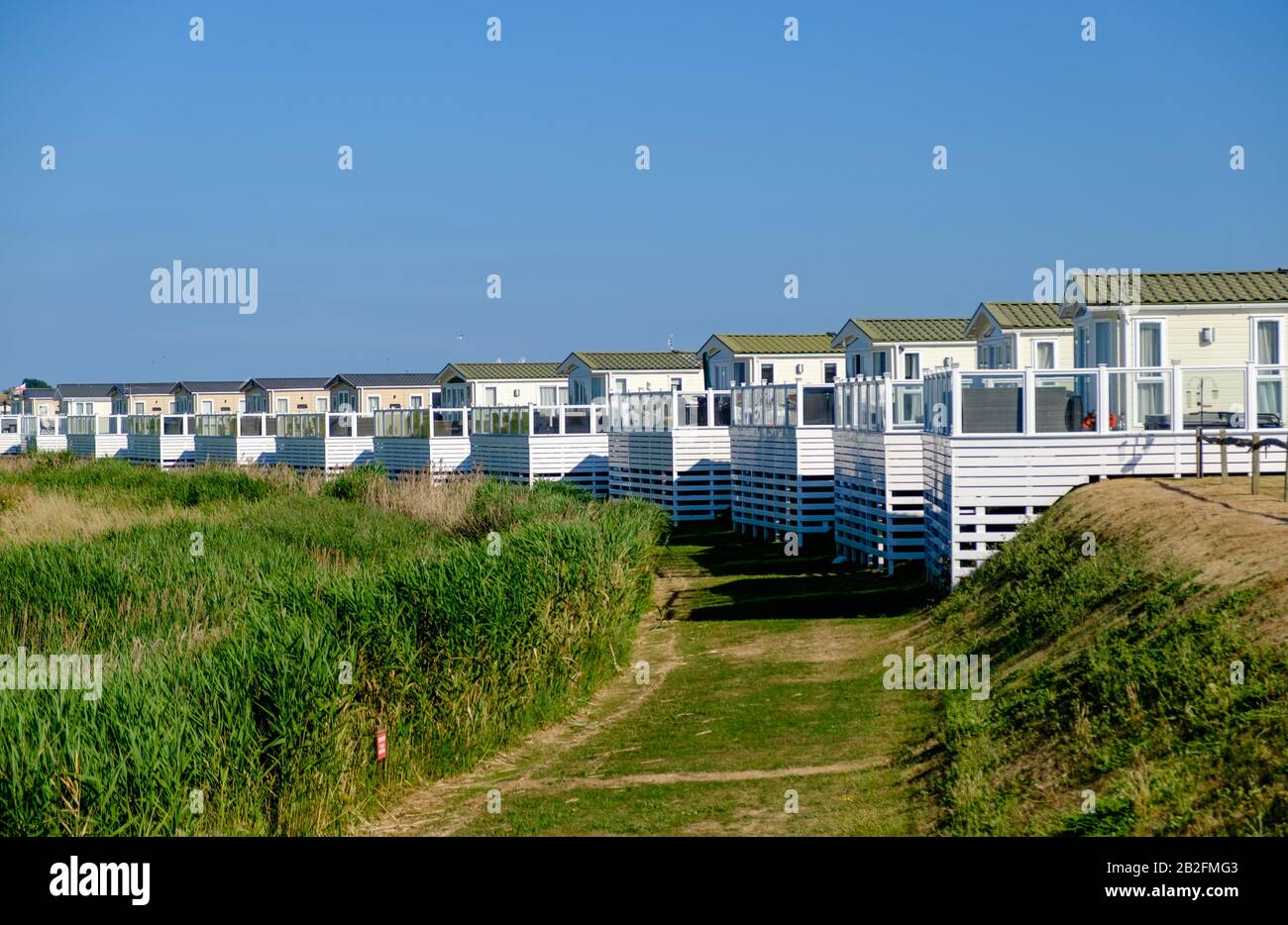 Curved grassy path in front of row of identical white static caravans ...
