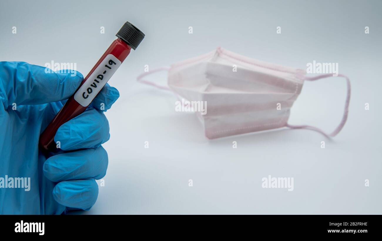 Surgical mask with coronavirus Covid 19 infected blood sample in tube ...