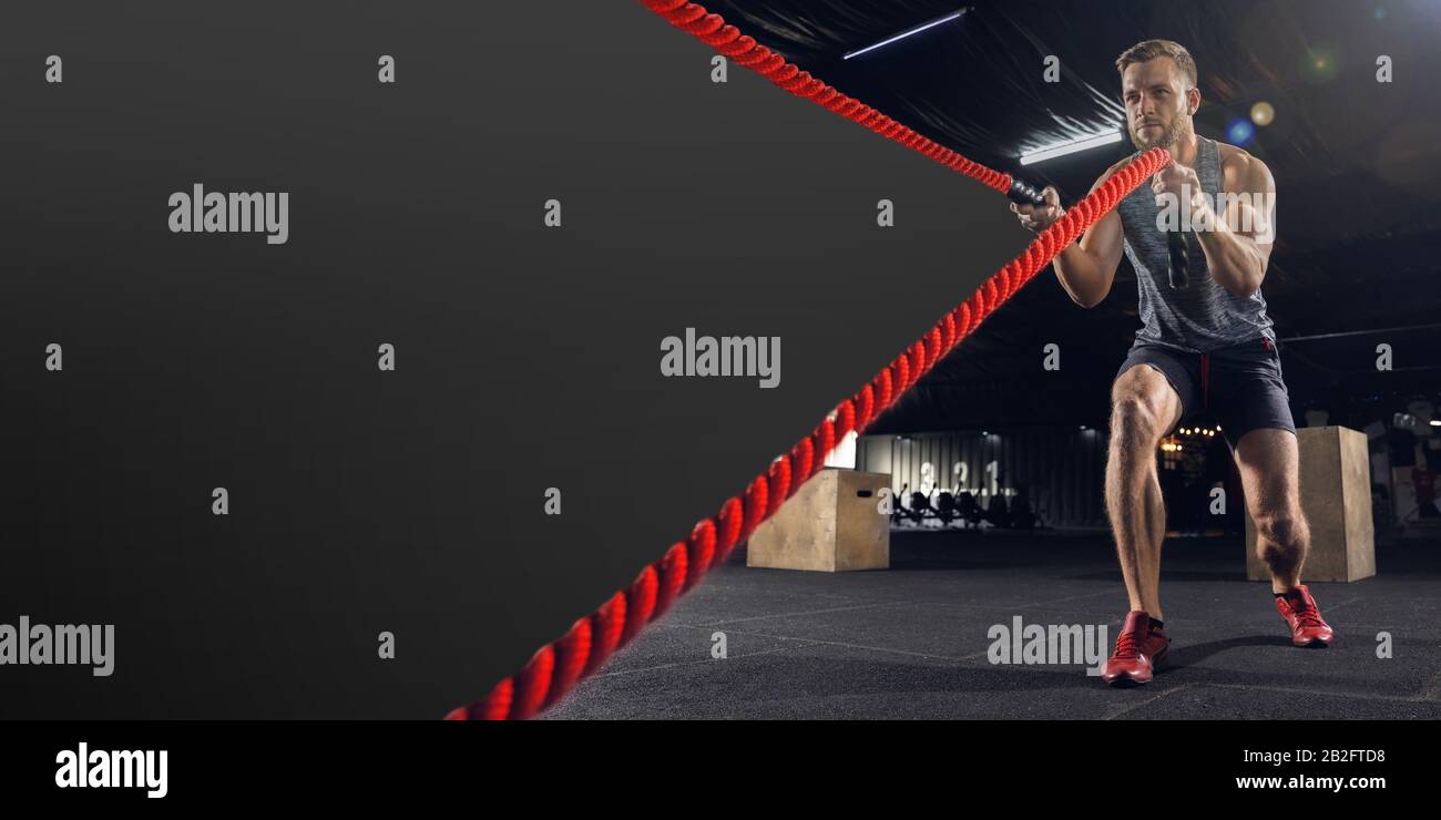 Young healthy man, athlete doing exercise with the ropes in the gym ...