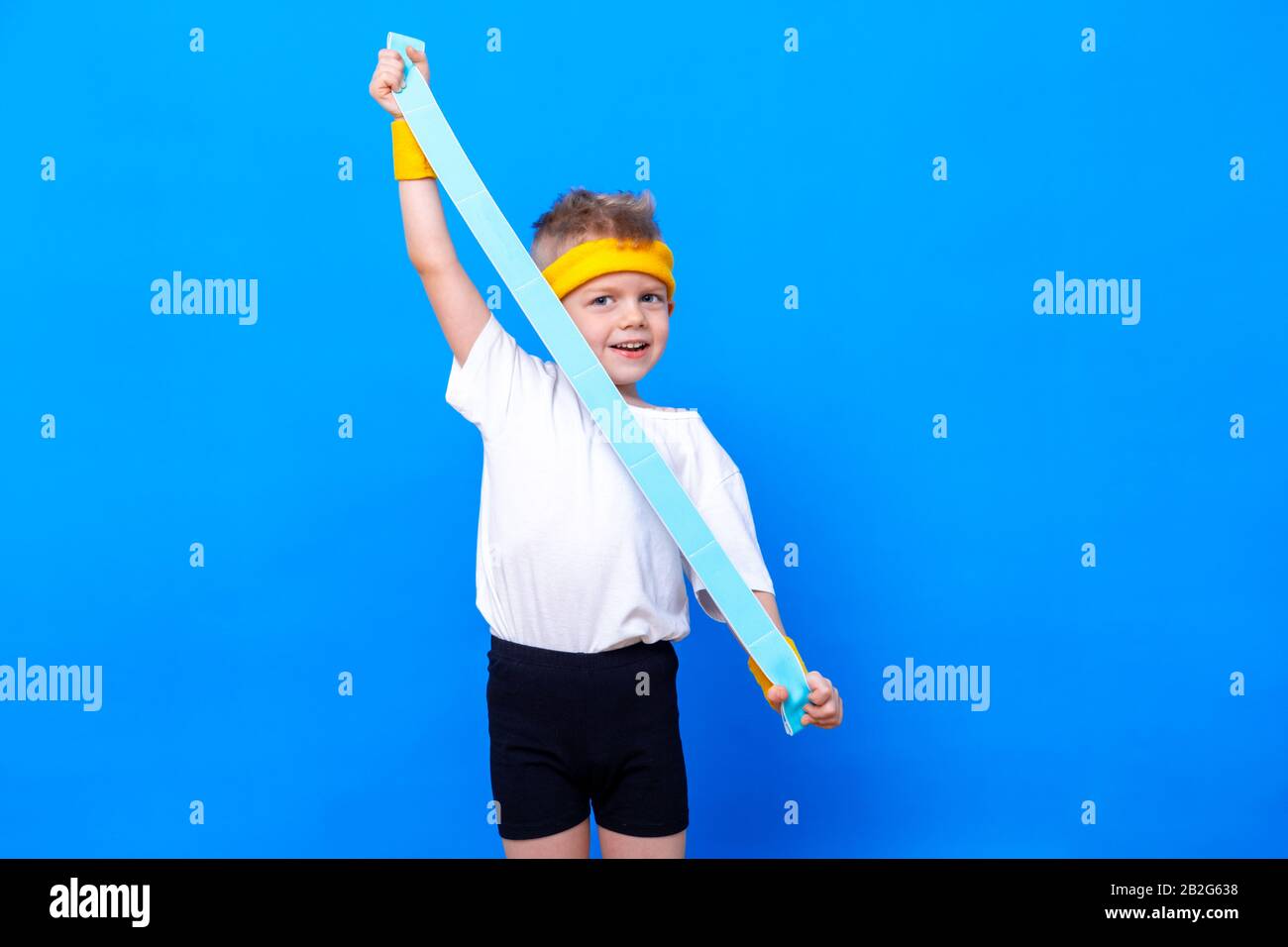 Sporty little boy with rubber fitness band over blue studio background ...