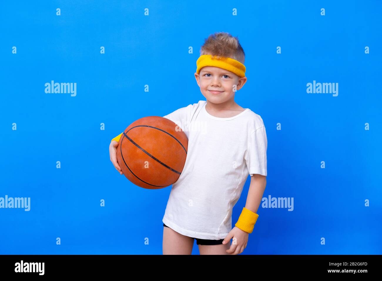 Sporty little boy with basketball ball over blue studio background. Gym ...