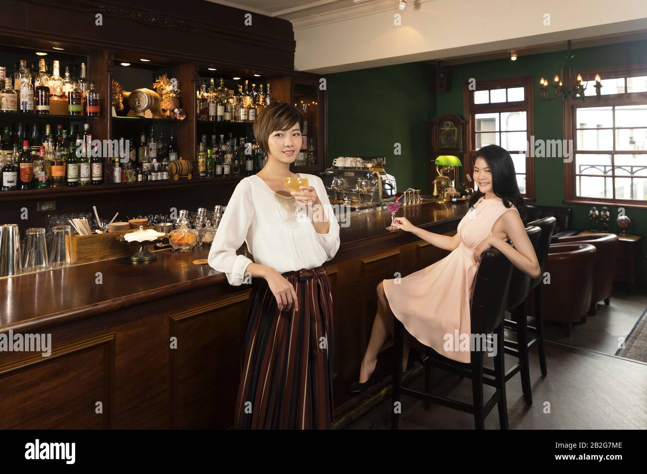 Two young women enjoying cocktails at bar Stock Photo - Alamy