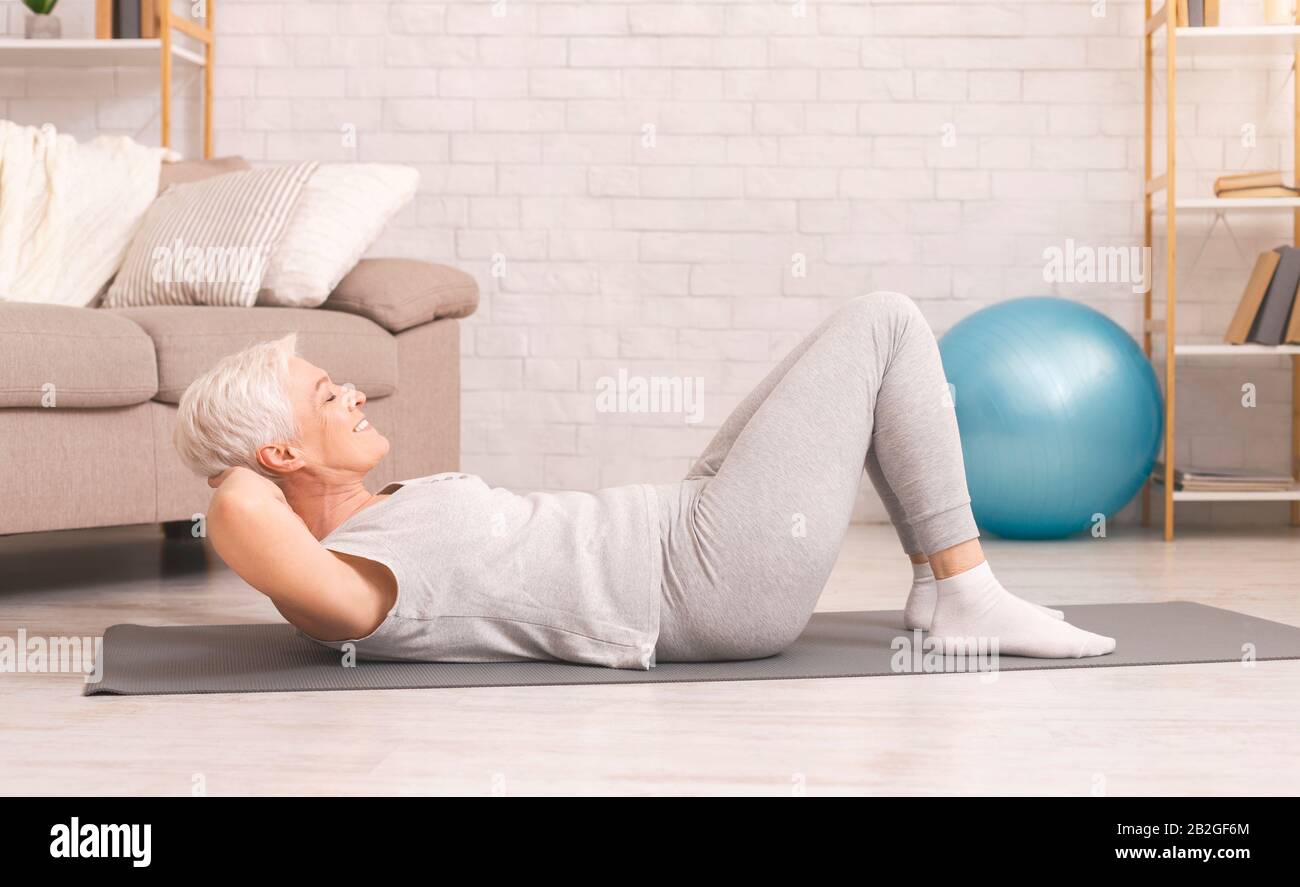 Positive senior lady doing abs exercise on floor at home Stock Photo ...
