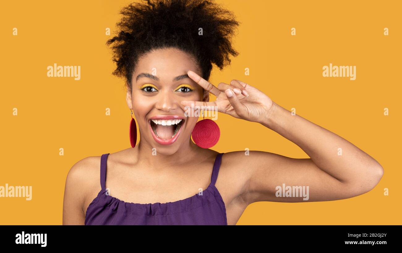 Excited afro girl showing v sign looking at camera Stock Photo - Alamy