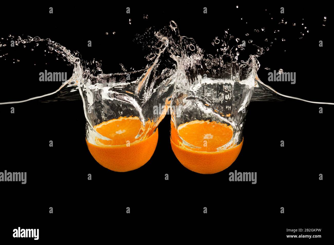 Sweet orange halves falling into transparent water with splash on black ...