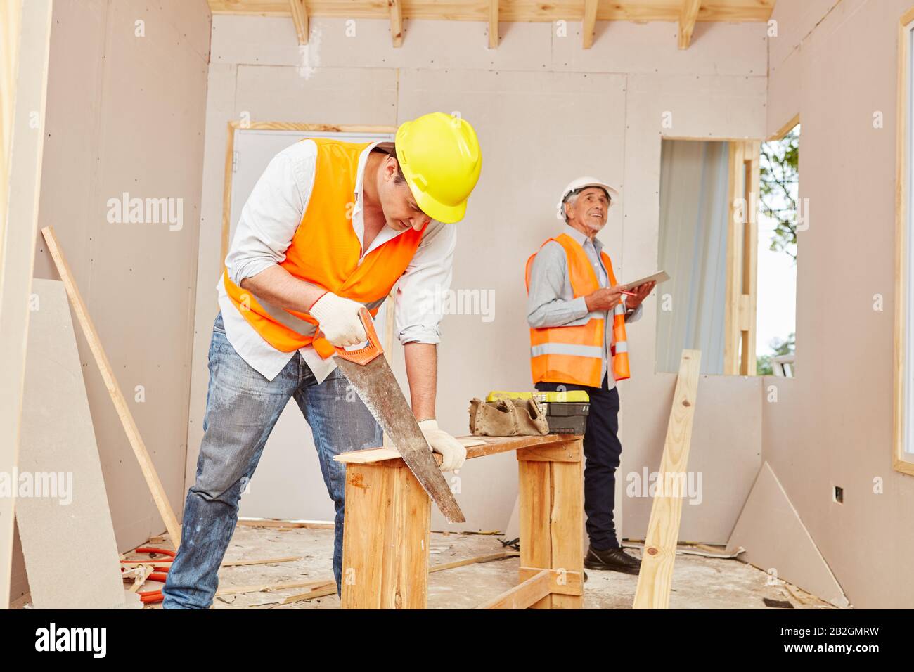 Craftsman with saw and architect using tablet computer during house ...