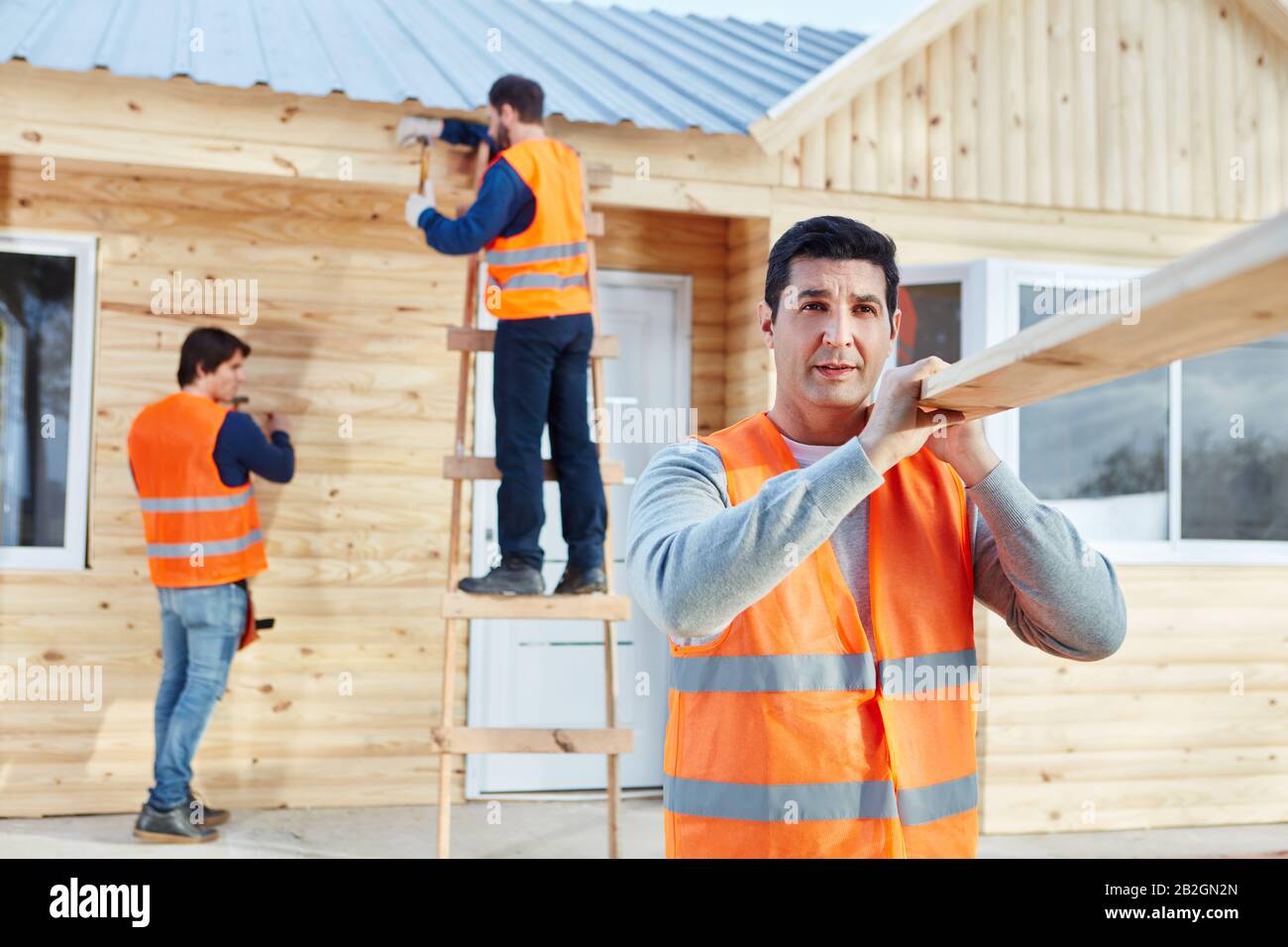 Three craftsmen build a wooden house together Stock Photo - Alamy