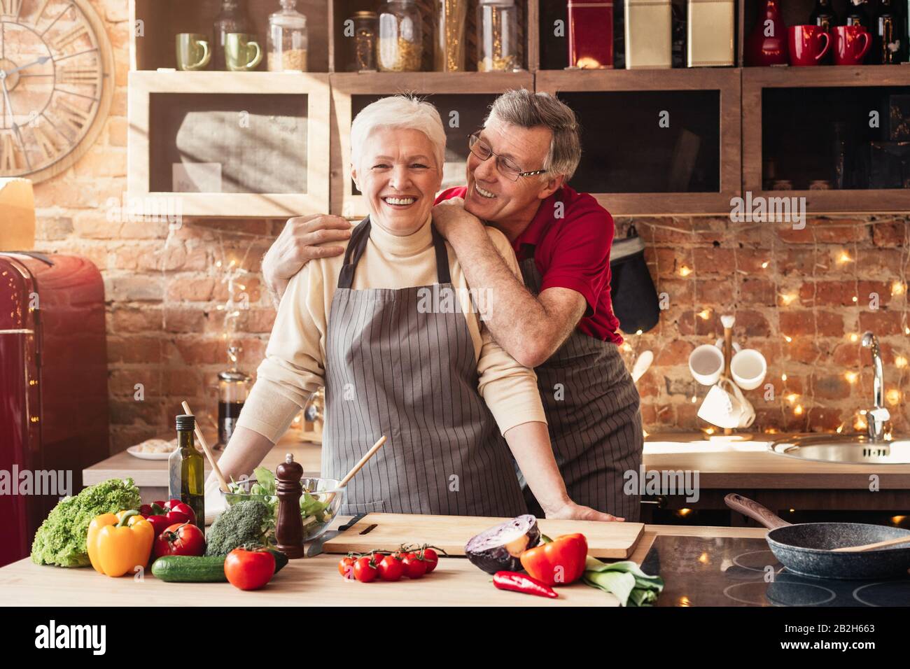 Happy Elderly Couple Embracing And Posing In Kitchen While Cooking ...