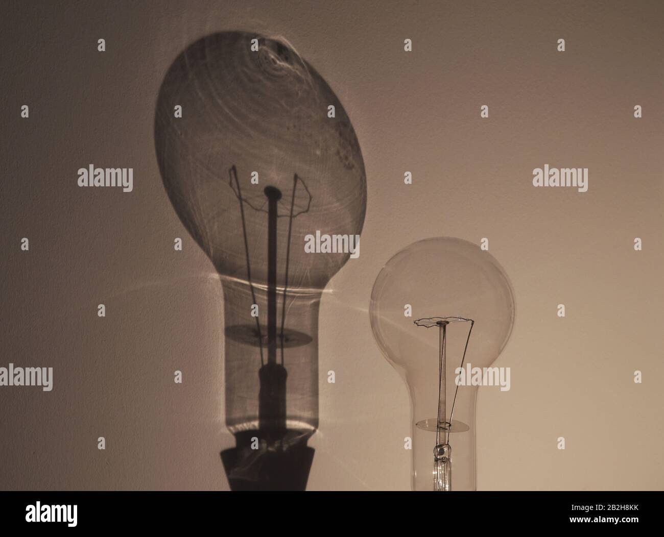 Large incandescent lightbulb lit by candlelight casting a shadow on the ...