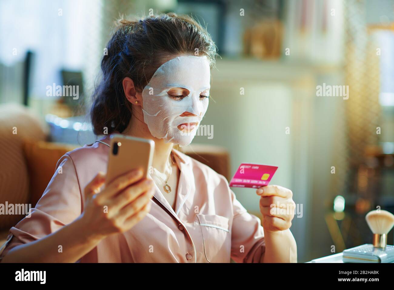 modern woman in pajamas with white sheet facial mask on face holding ...