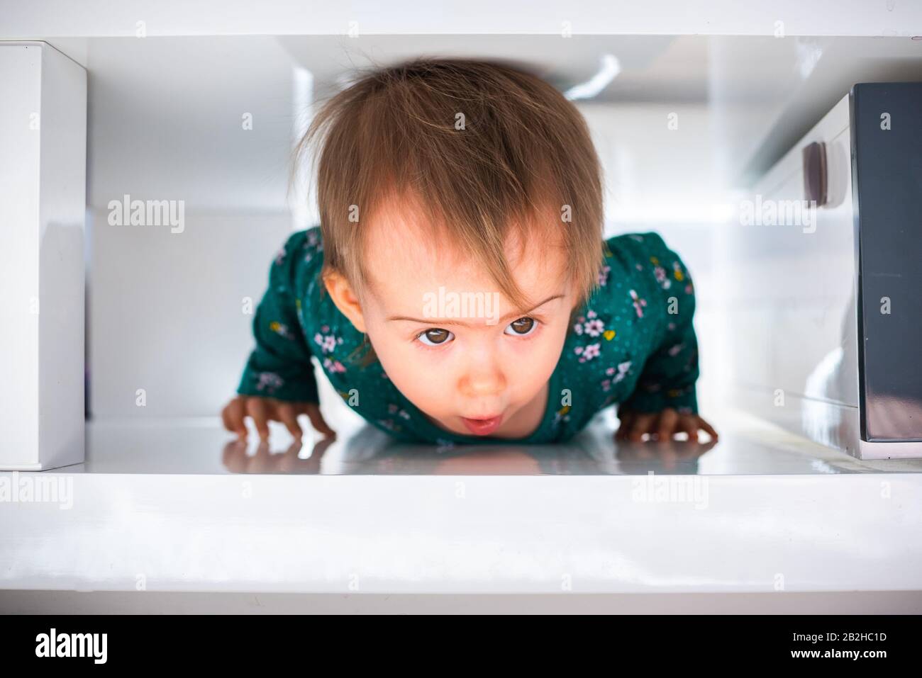 Cute caucasian baby girl crawl through tight space under coffee table ...